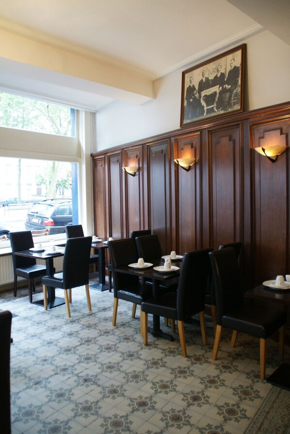 Uma sala de jantar com painéis de madeira, cadeiras pretas e mesas preparadas para refeições.