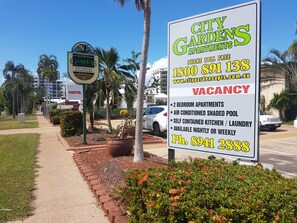 Placa do City Gardens Apartments anunciando vagas, comodidades como cozinha privativa e informações de contato.
