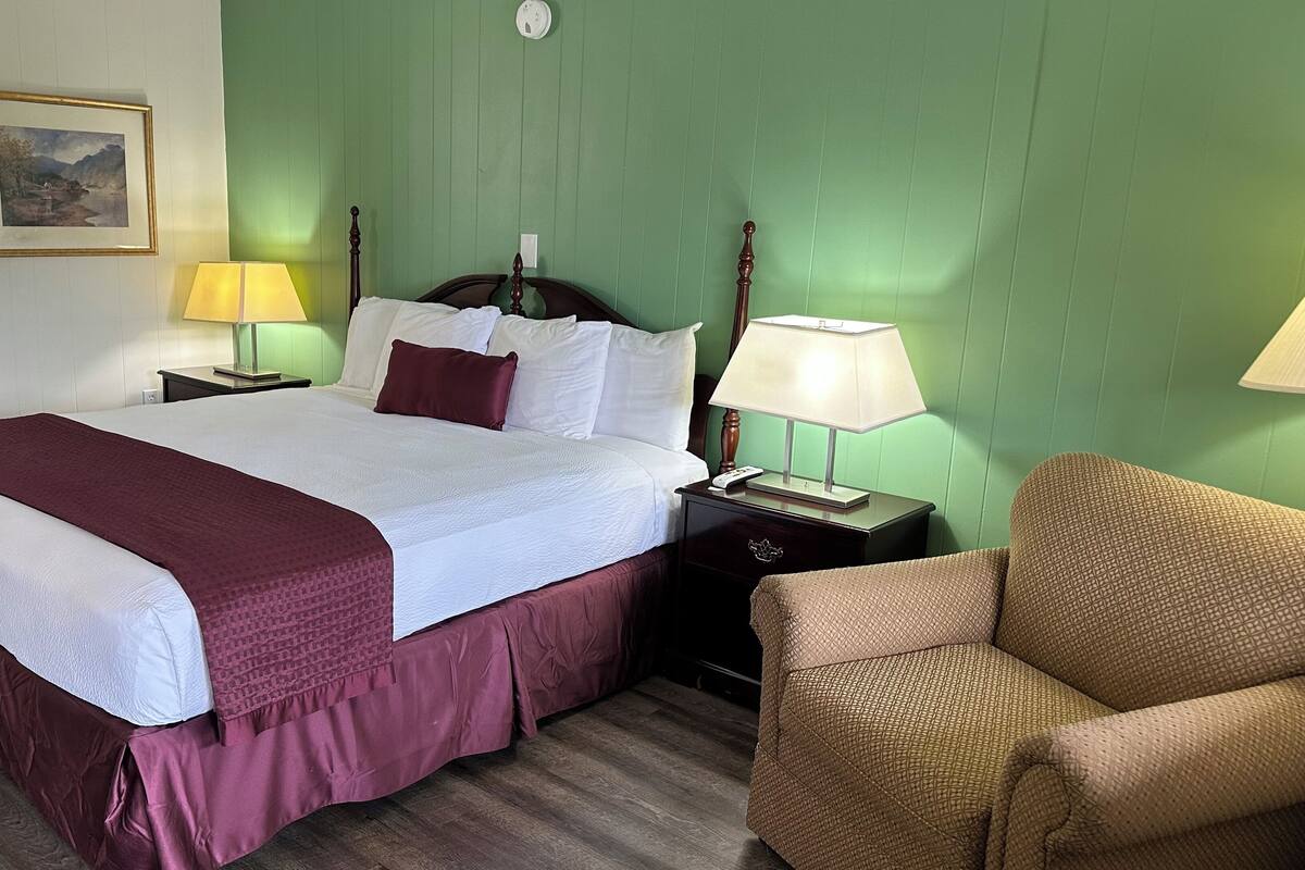 Quarto de hotel com uma cama grande, duas mesas de cabeceira, uma cadeira e uma parede verde.
