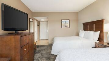 Quarto de hotel com televisão de tela plana sobre uma cômoda de madeira, duas camas com lençóis brancos, um quadro na parede e uma cabeceira de madeira.