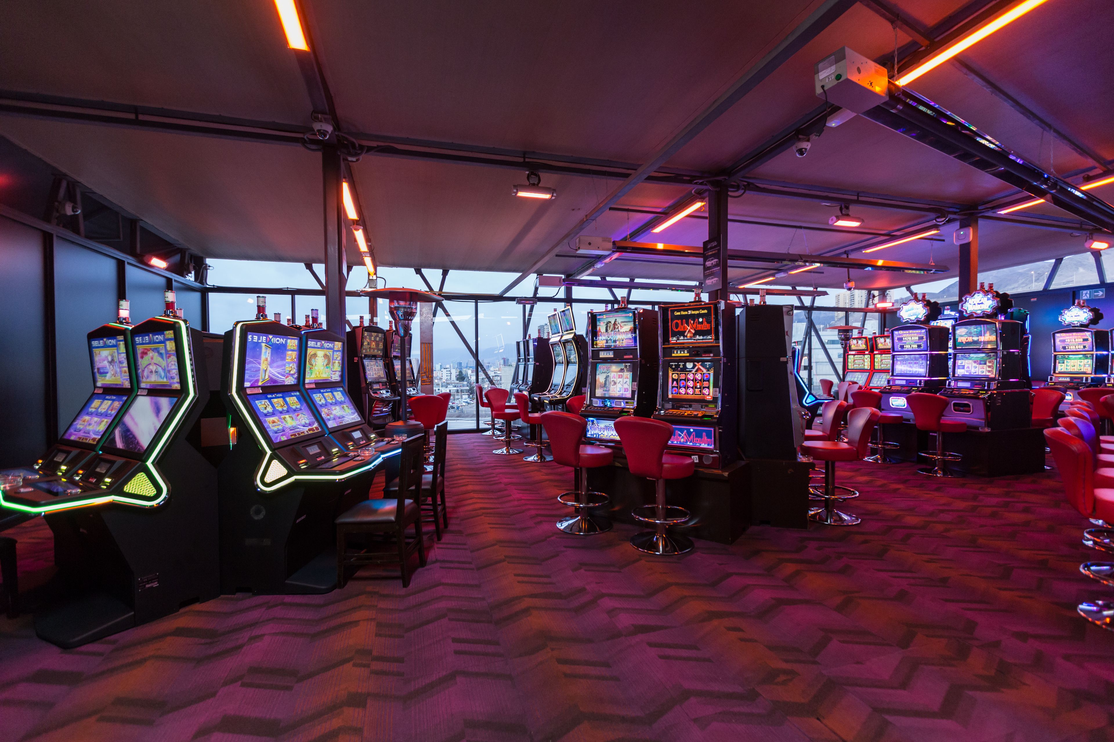Uma área de jogos com várias máquinas de arcade, banquetas vermelhas e um tapete estampado.
