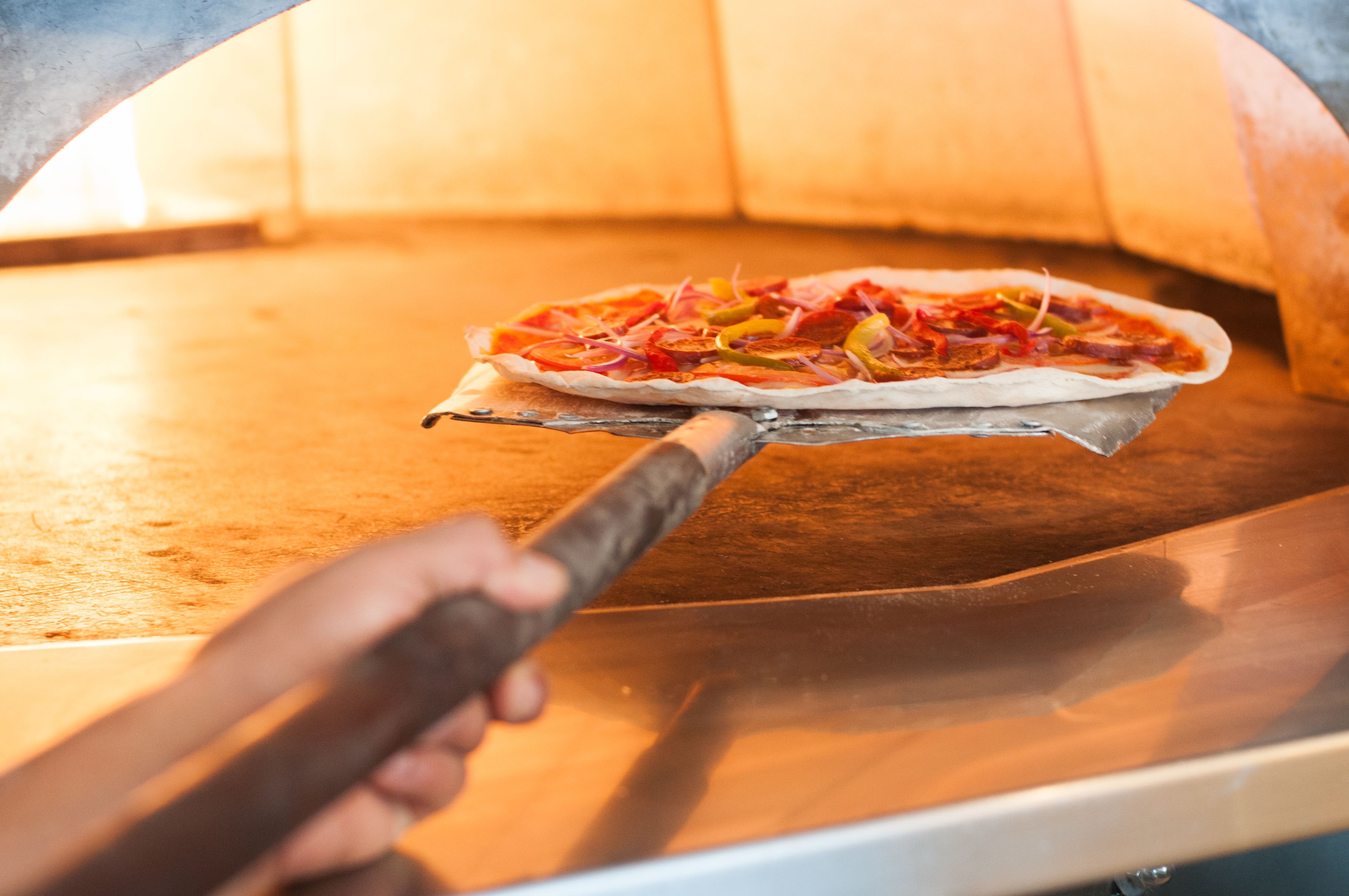 Pizza sendo retirada de um forno de tijolos.