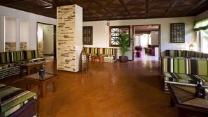 Um hall amplo com teto alto, um pilar de pedra e uma área de estar com sofás listrados e mesas.