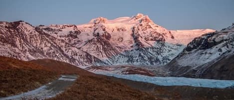 Paisagem montanhosa com pico coberto de neve e um rio serpenteando por um vale.