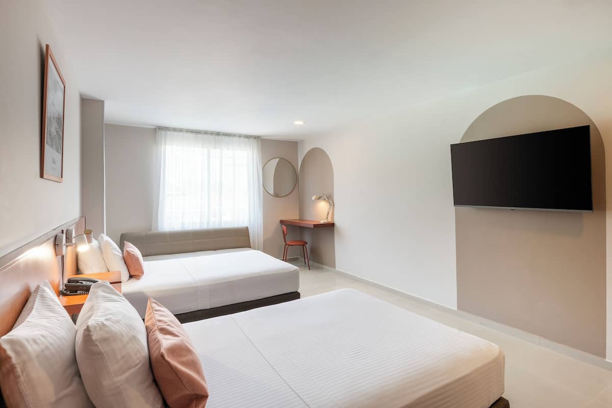 Quarto de hotel com duas camas, uma escrivaninha, uma cadeira, uma televisão e janela com cortinas.
