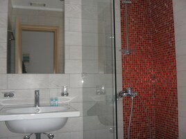 Casa de banho com lavatório branco, espelho e chuveiro com azulejos de mosaico vermelhos.