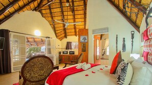 Quarto amplo com cama grande, uma cadeira de madeira, escrivaninha com computador e pequeno espaço de cozinha.