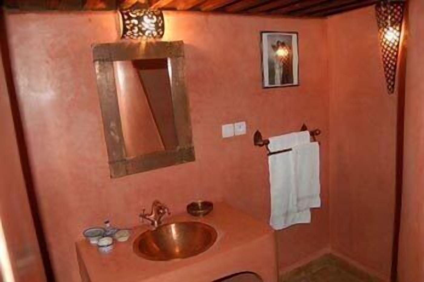 Casa de banho com lavatório de cobre, espelho e toalha pendurada num suporte.