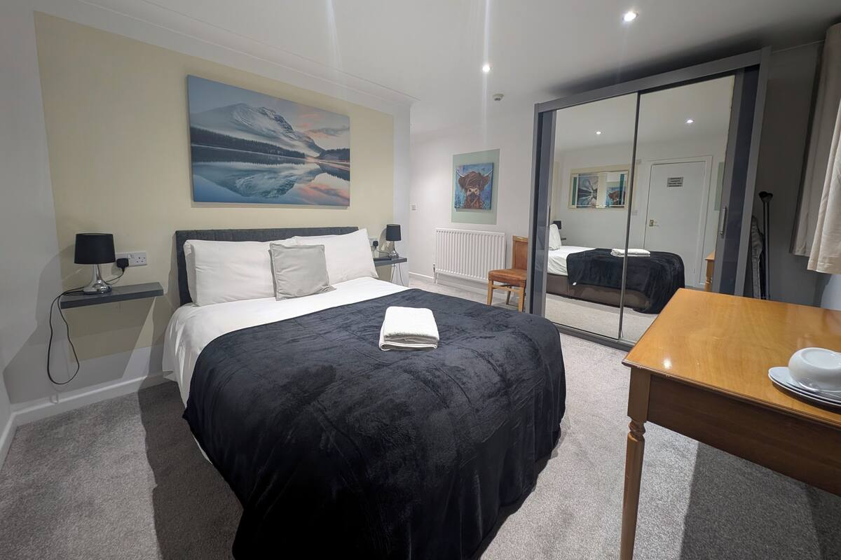 Quarto de hotel com cama, mesa de cabeceira, luminária, obra de arte na parede e porta deslizante.