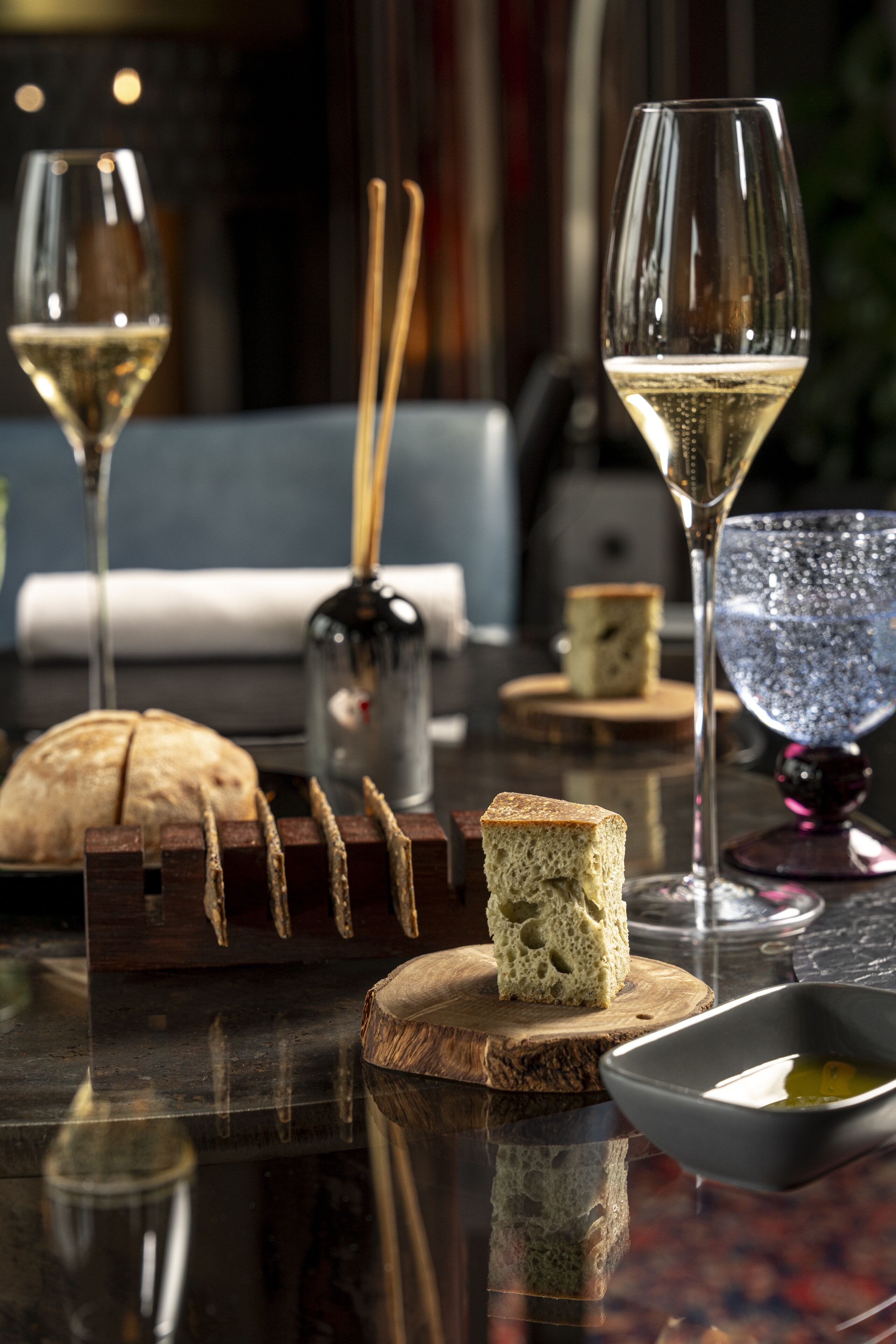 Uma mesa com um pão, um copo de vinho branco, um copo de água com gás e uma pequena tigela de azeite.