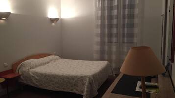 Quarto de hotel com uma cama, mesa de cabeceira, abajur e janela com cortinas.