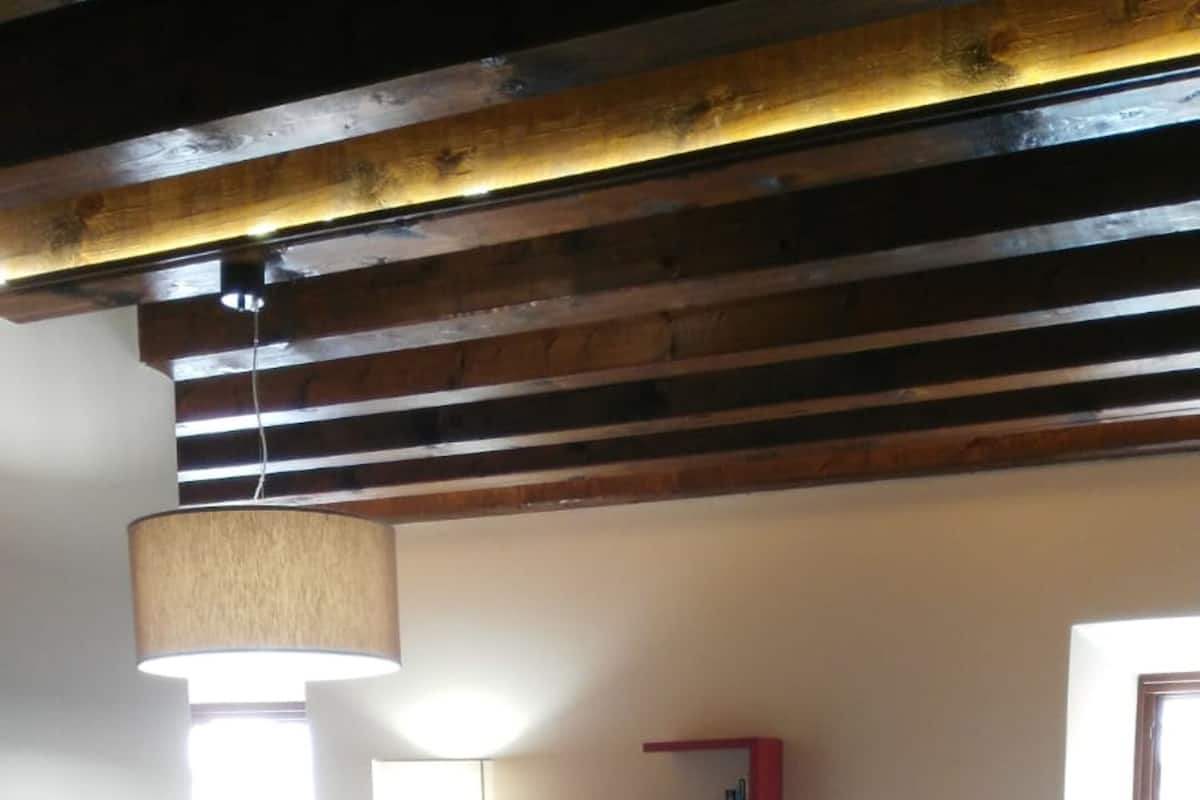 Uma área de refeições com mesa de vidro, quatro cadeiras, televisão em móvel e estante vermelha.