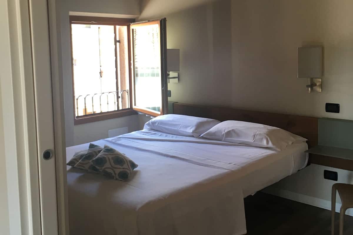 Quarto com cama, janela, cadeira e luminária fixada na parede.