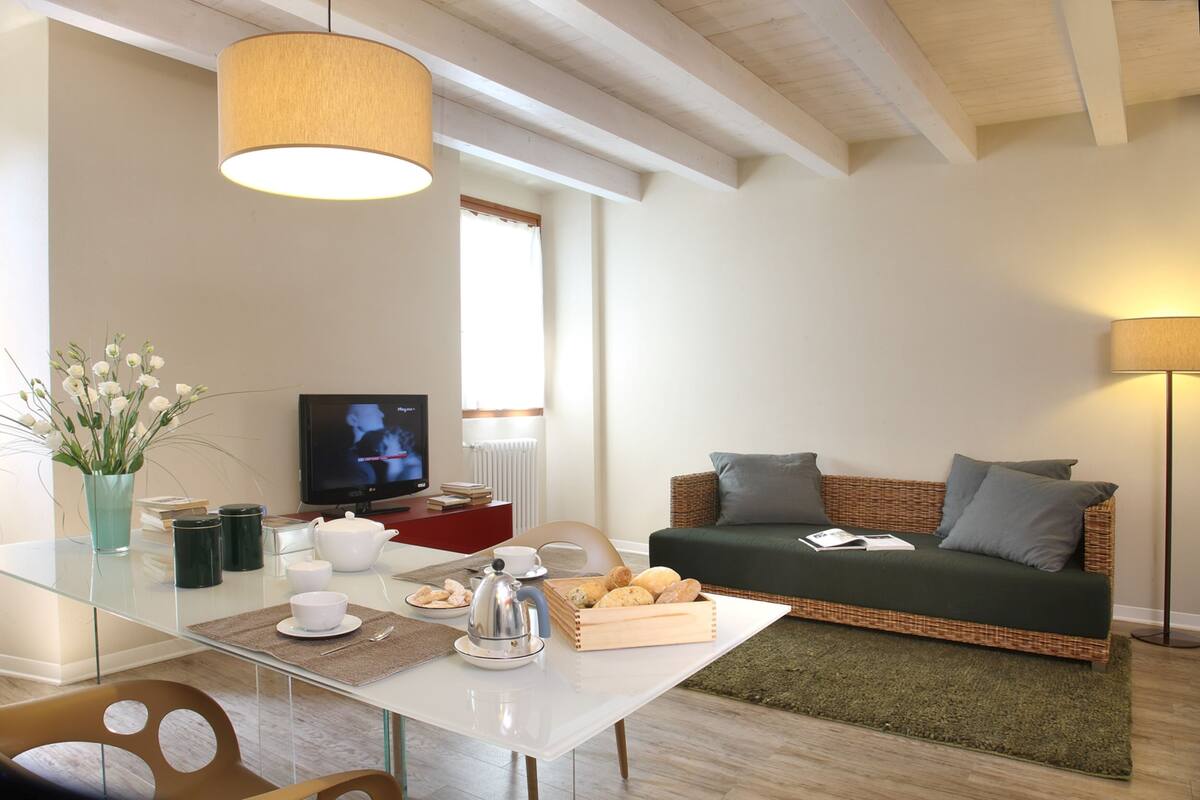 Uma sala de estar moderna com uma mesa de jantar de vidro, sofá de vime e uma televisão.