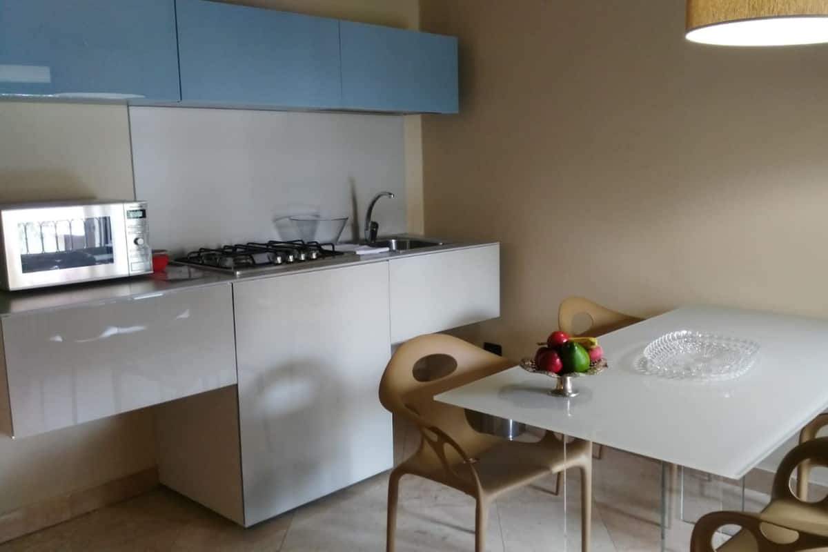 Uma cozinha moderna com ilha branca, armários azuis e um espaço de refeições com mesa e cadeiras brancas.