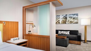 Quarto de hotel com cama, escrivaninha com luminária, sofá e um quadro na parede.