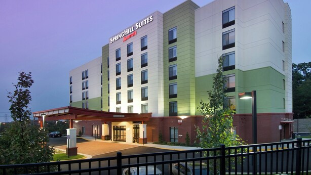 Um hotel com vários andares, teto plano, entrada coberta e uma placa indicando ser um SpringHill Suites Marriott.