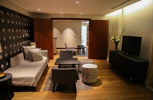 Uma sala de estar moderna com um sofá, uma mesa de centro, pufes, uma TV e uma área de jantar ao fundo.