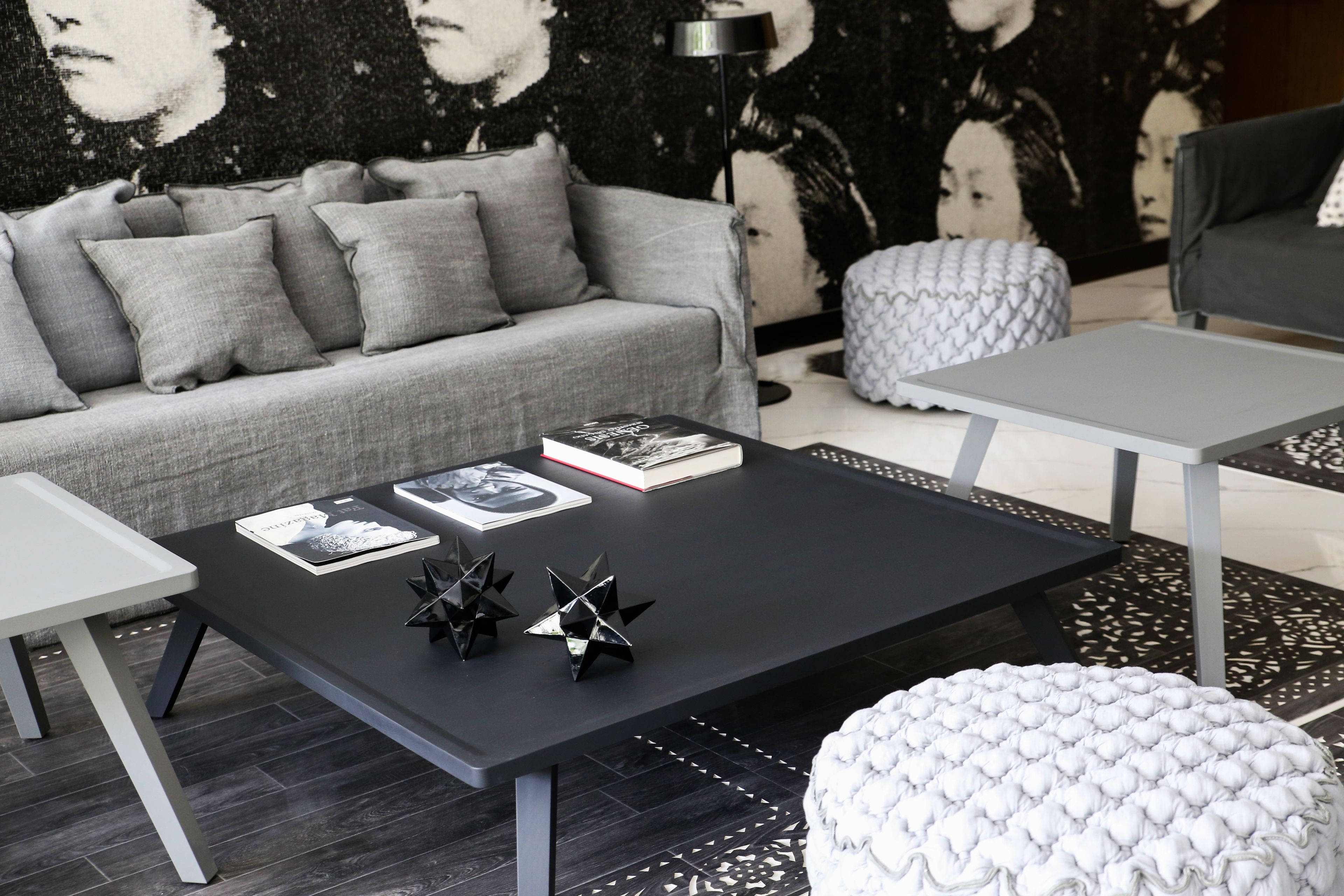 Uma sala de estar moderna com um sofá cinzento, uma mesa de centro preta com livros e objetos decorativos, e um tapete estampado.