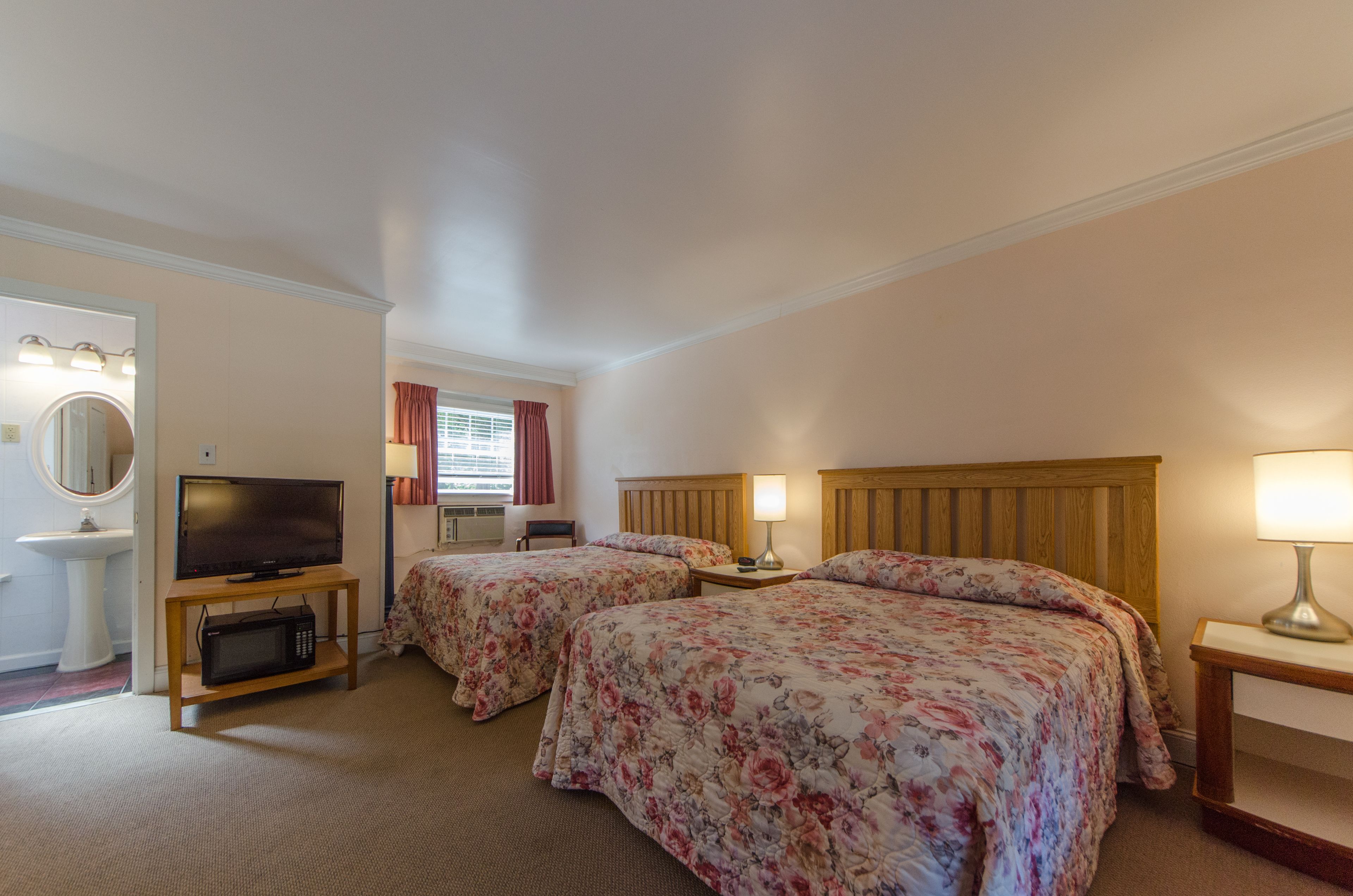 Quarto de hotel com duas camas, uma televisão sobre um suporte, uma pia e um espelho.