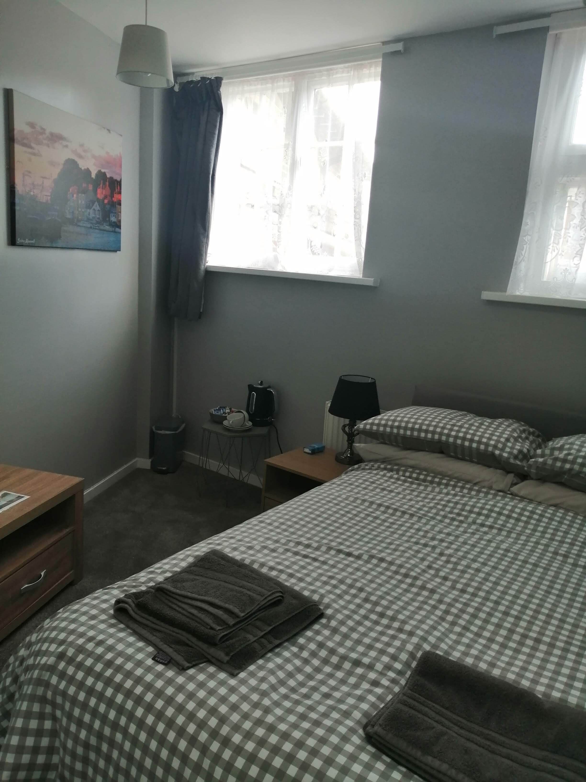 Quarto com duas camas, mesa de cabeceira, luminária, janela com cortinas e um quadro na parede.