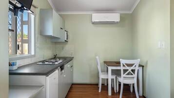 Cozinha compacta com fogão a gás, armários brancos, mesa de jantar com duas cadeiras e um aparelho de ar condicionado fixado na parede.