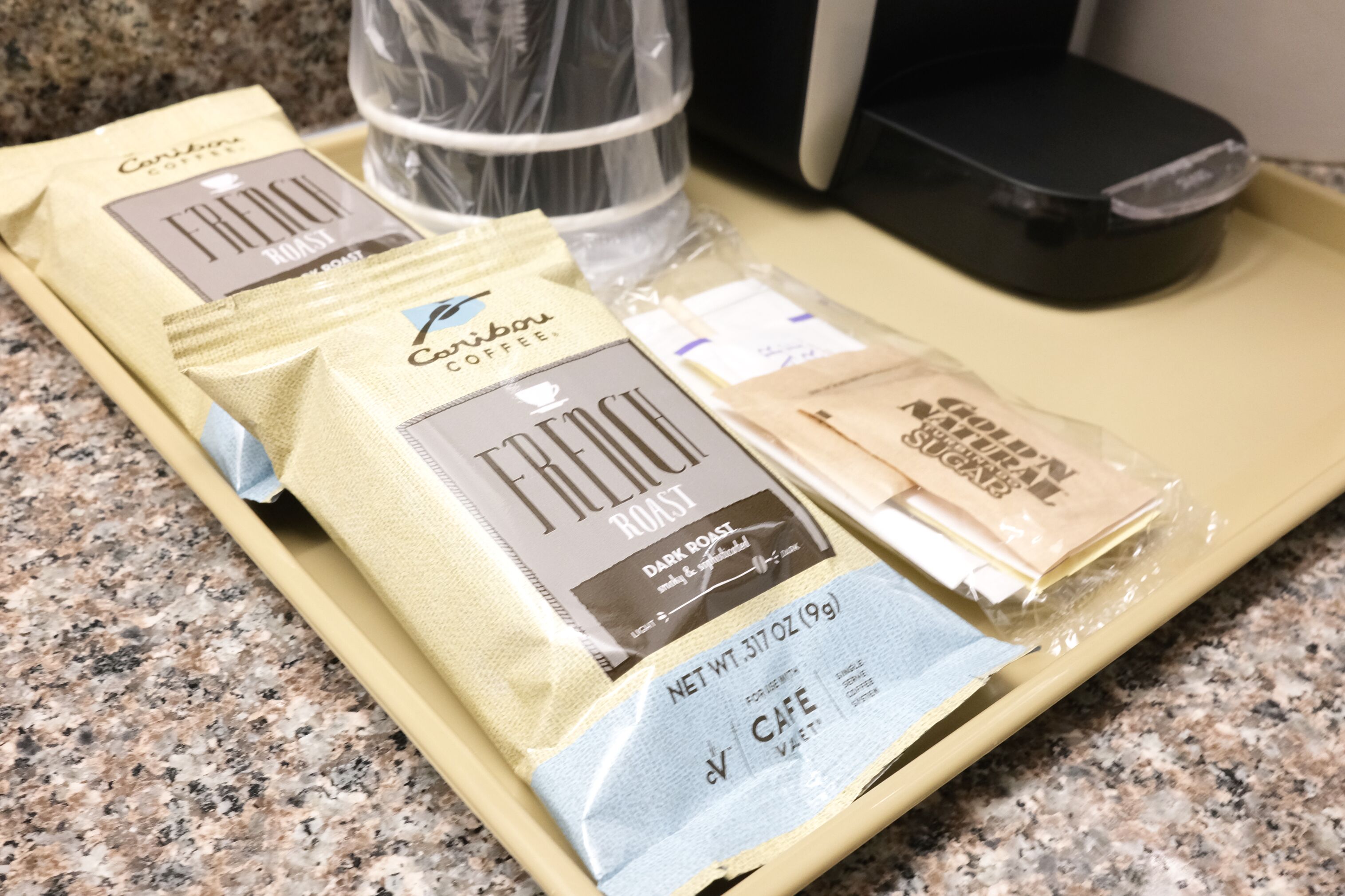 Uma bandeja com sacos de café rotulados 'French Roast' e 'Cafe' sobre uma bancada de granito.