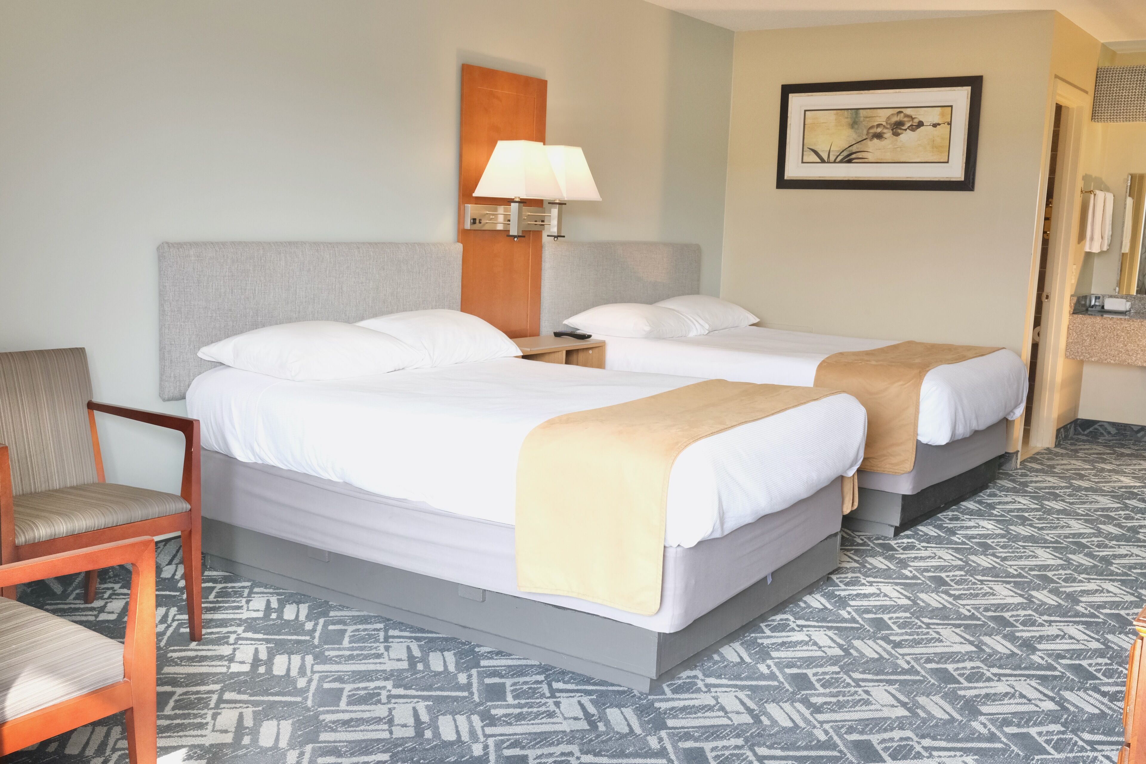 Quarto de hotel com duas camas, uma cadeira, um abajur e um quadro na parede.