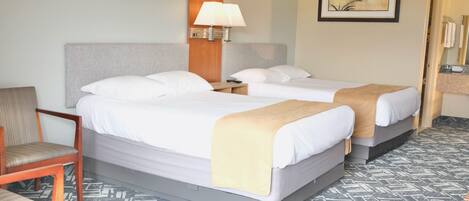 Quarto de hotel com duas camas, uma cadeira, um abajur e um quadro na parede.