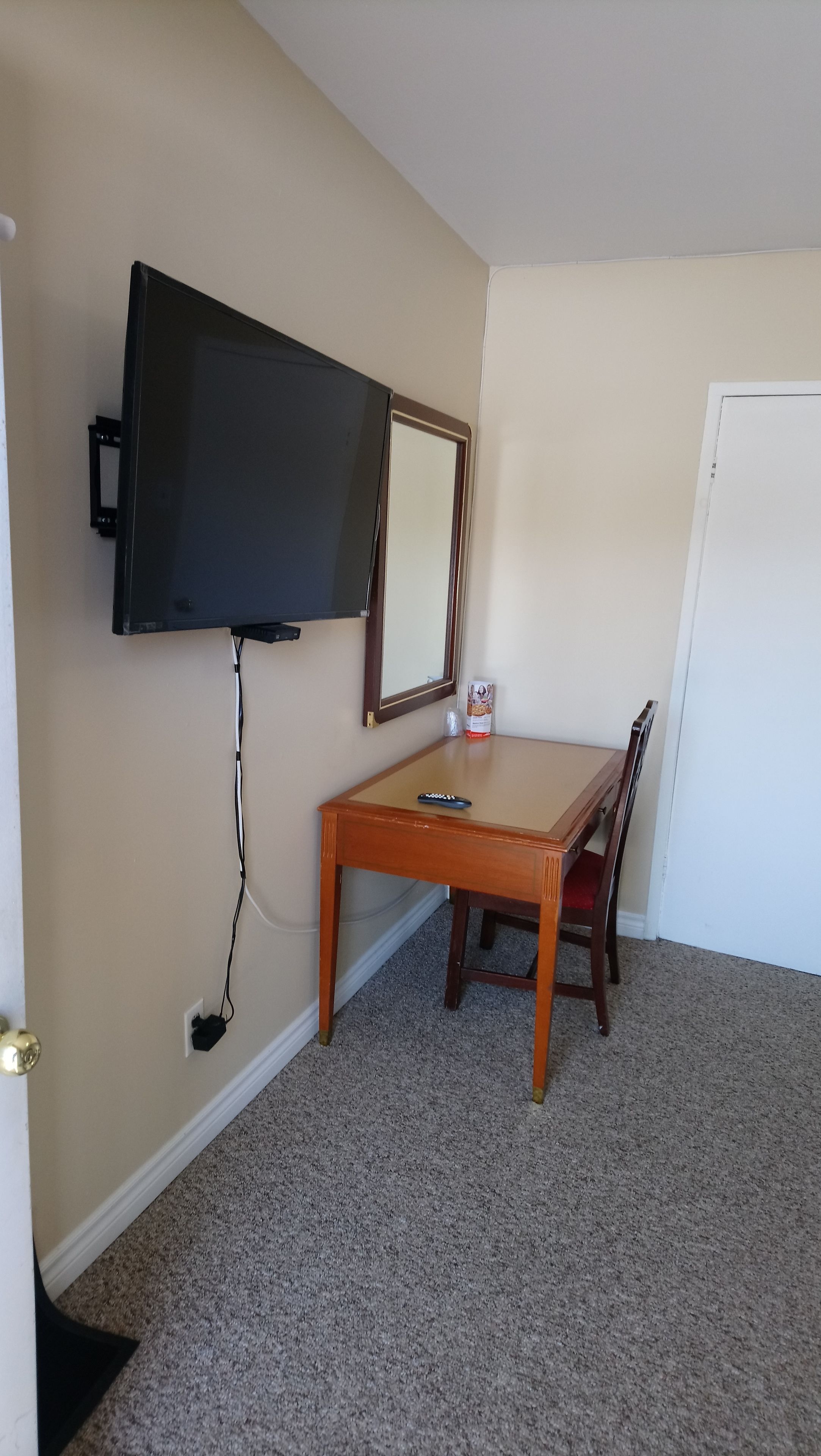 Quarto com televisão na parede, uma mesa de madeira com uma cadeira e uma porta.