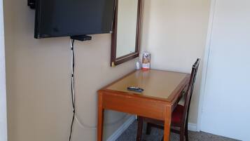 Quarto com televisão na parede, uma mesa de madeira com uma cadeira e uma porta.