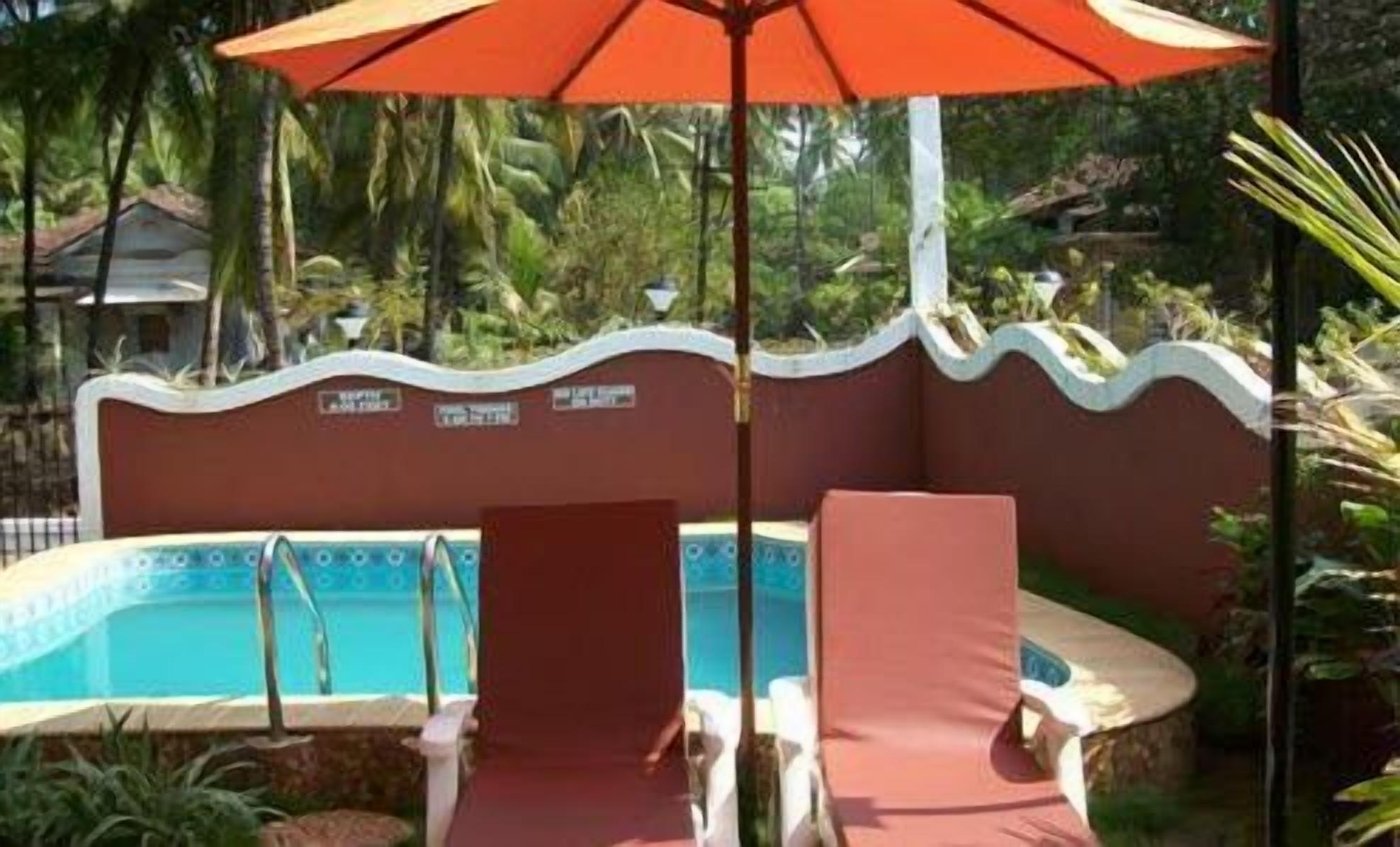 Uma área de piscina com um guarda-sol vermelho, duas espreguiçadeiras e uma piscina com interior azul.