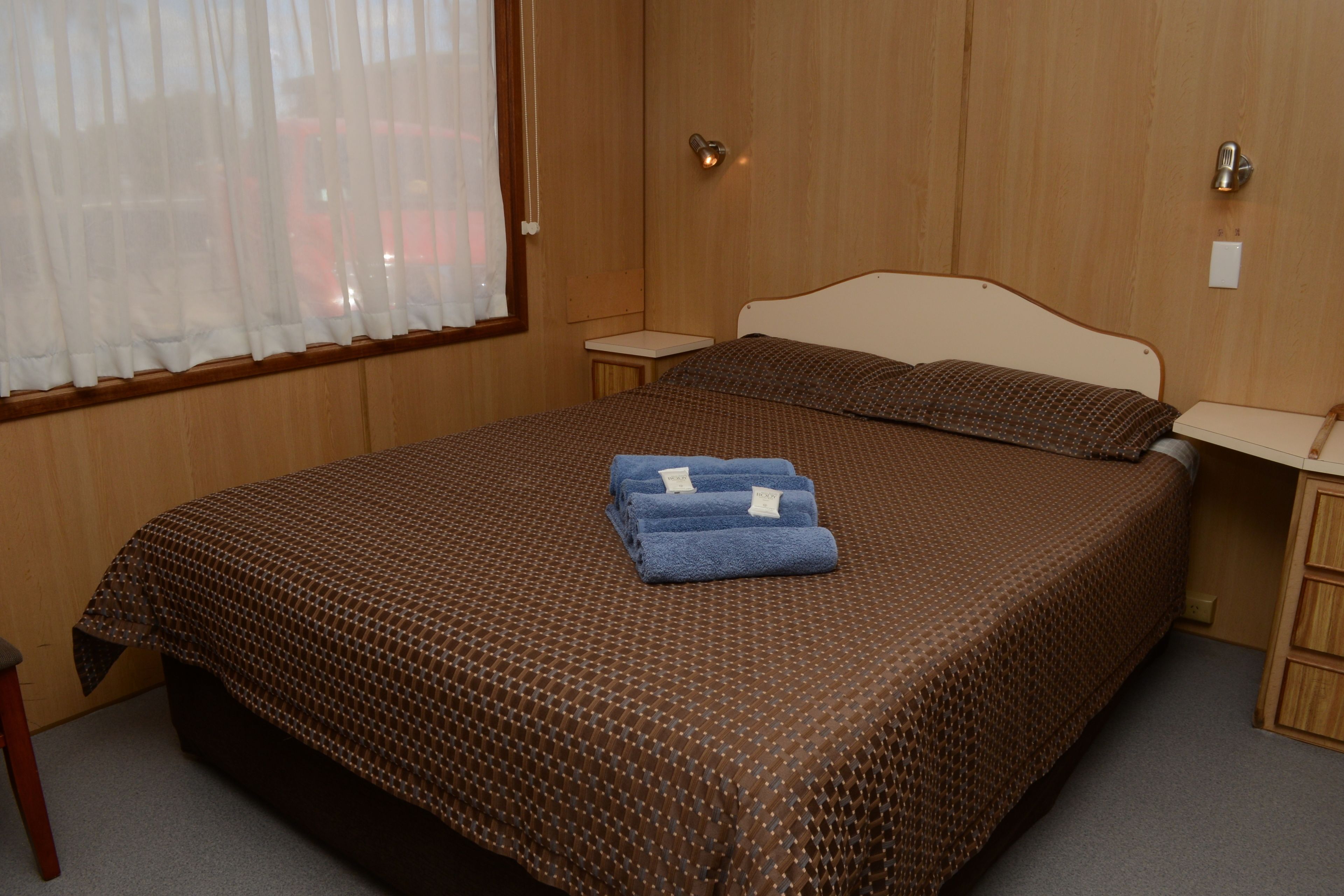 Quarto com uma cama grande, cabeceira de madeira, duas mesas de cabeceira e uma janela com cortinas leves.