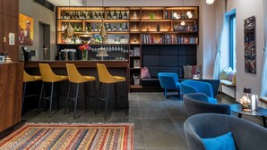 Um espaço de bar com bancos, prateleiras cheias de garrafas e livros. Há cadeiras e um tapete na área de estar.