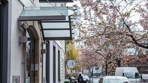 Uma rua estreita com carros estacionados e um hotel chamado "MRAK HOTEL", com uma placa sobre a entrada.