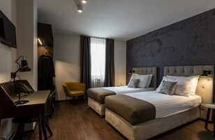 Quarto de hotel com duas camas, uma escrivaninha com telefone, uma cadeira e um grande mural na parede.