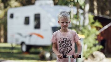Criança num triciclo com uma motorhome branca ao fundo.