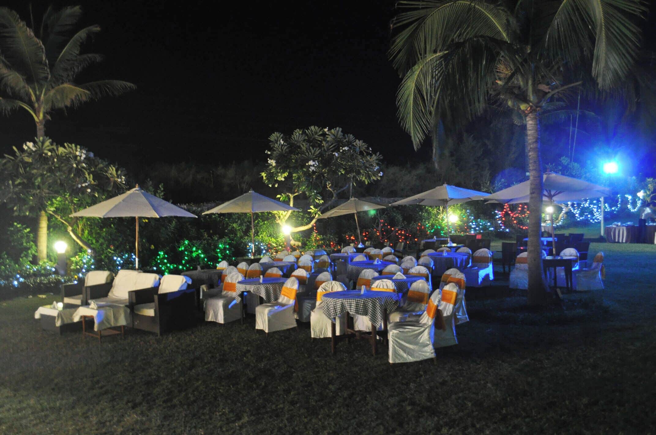 Um evento ao ar livre com fileiras de cadeiras e mesas, decorado com luzes e guarda-sóis.