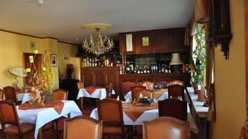 Restaurante com mesas preparadas para refeições, área de bar e um candelabro.