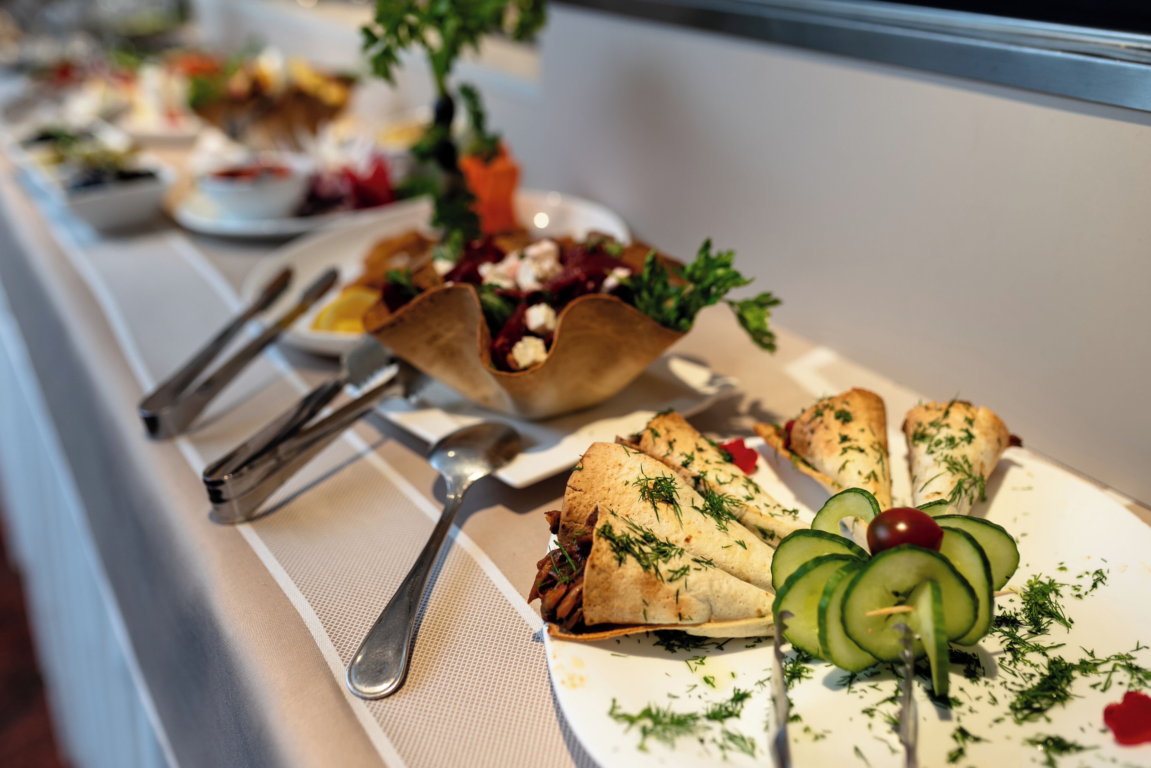Uma mesa de buffet com diversos pratos, incluindo uma salada com pepinos e tomates cereja, e um prato com espeto de pepino e tomate cereja.