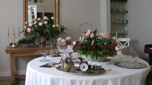Uma mesa de jantar posta com talheres, pratos e copos, rodeada por arranjos florais e um espelho.