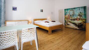 Quarto com cama de madeira, paredes brancas, mesa de vidro e cadeira branca.