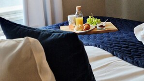 Quarto de hotel com uma cama, bandeja de café da manhã com croissants, uvas, suco e uma garrafa de suco de laranja.
