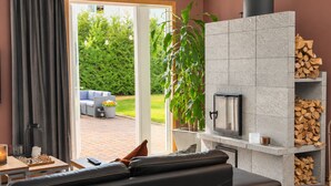 Uma sala de estar com lareira, sofá, mesa de centro e vista para um jardim através de uma porta de vidro.