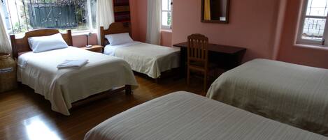 Quarto com três camas individuais, uma escrivaninha de madeira, uma cadeira e um espelho na parede.
