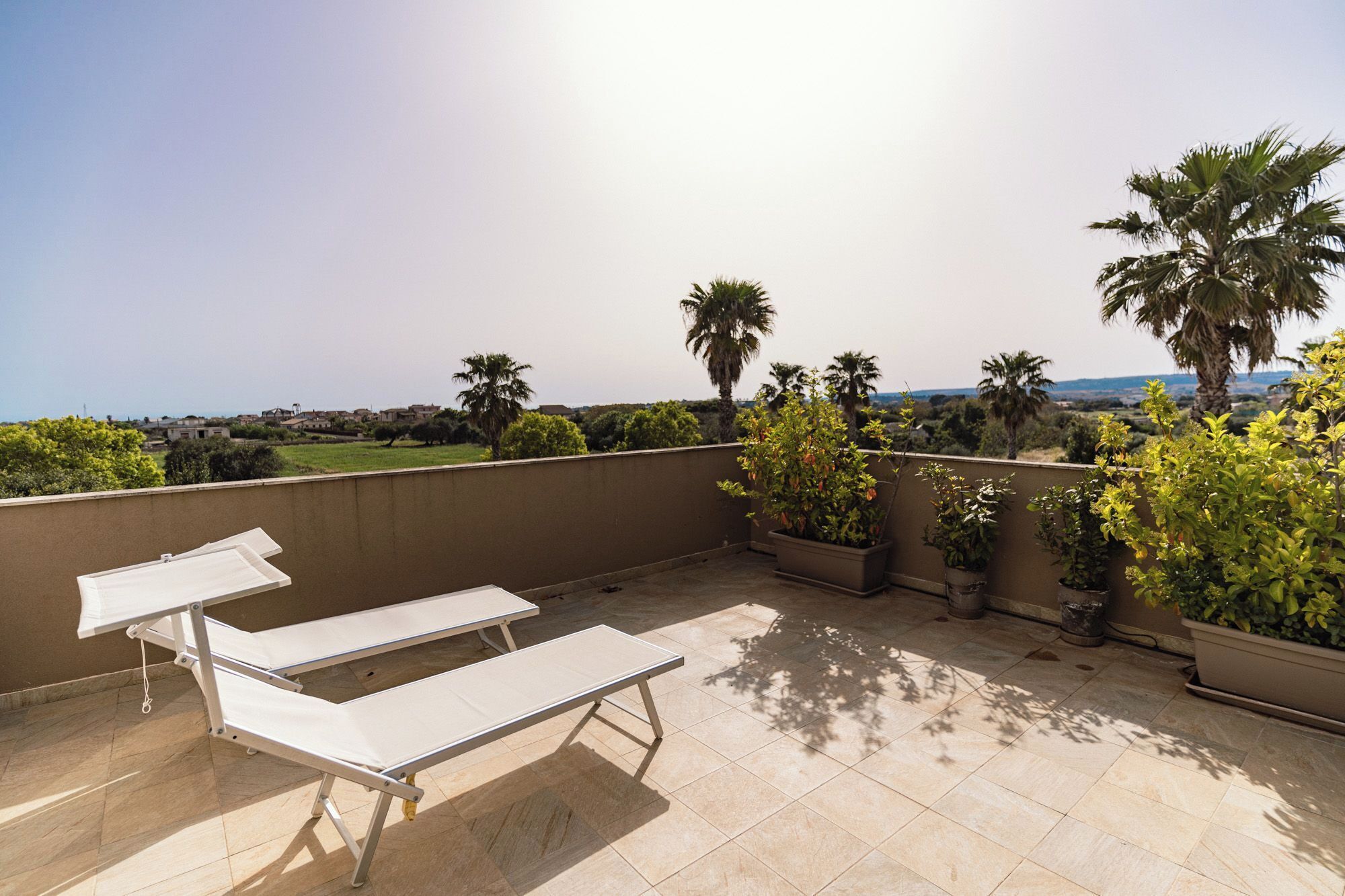 Terraço no telhado com duas poltronas brancas, plantas em vasos e vista para a paisagem.