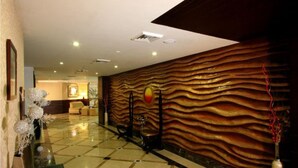 Um saguão de hotel com piso de mármore, balcão de recepção, parede com padrão ondulado e um vaso decorativo com flores vermelhas.