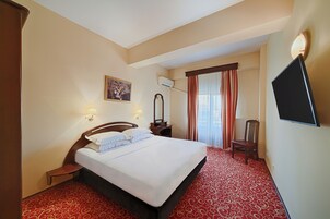 Quarto de hotel com cama, escrivaninha, cadeira, televisão e um quadro na parede.