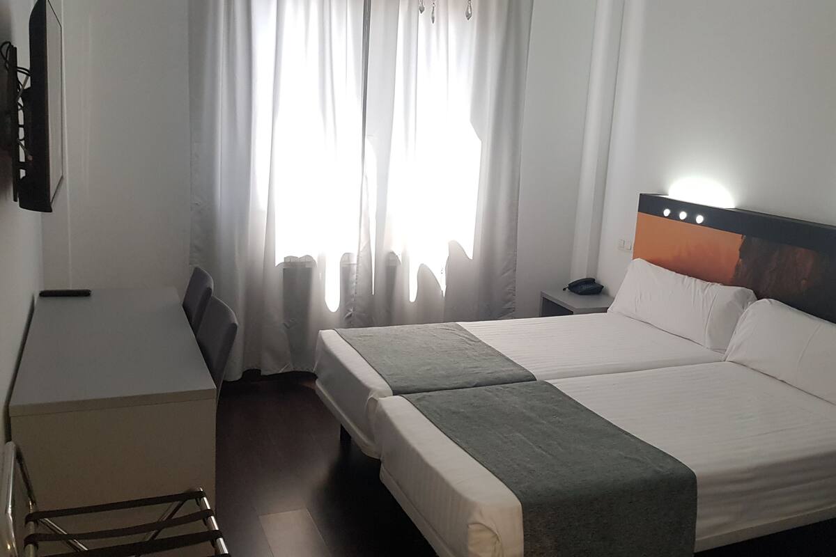 Quarto de hotel com cama, mesa de cabeceira, abajur e uma cadeira.