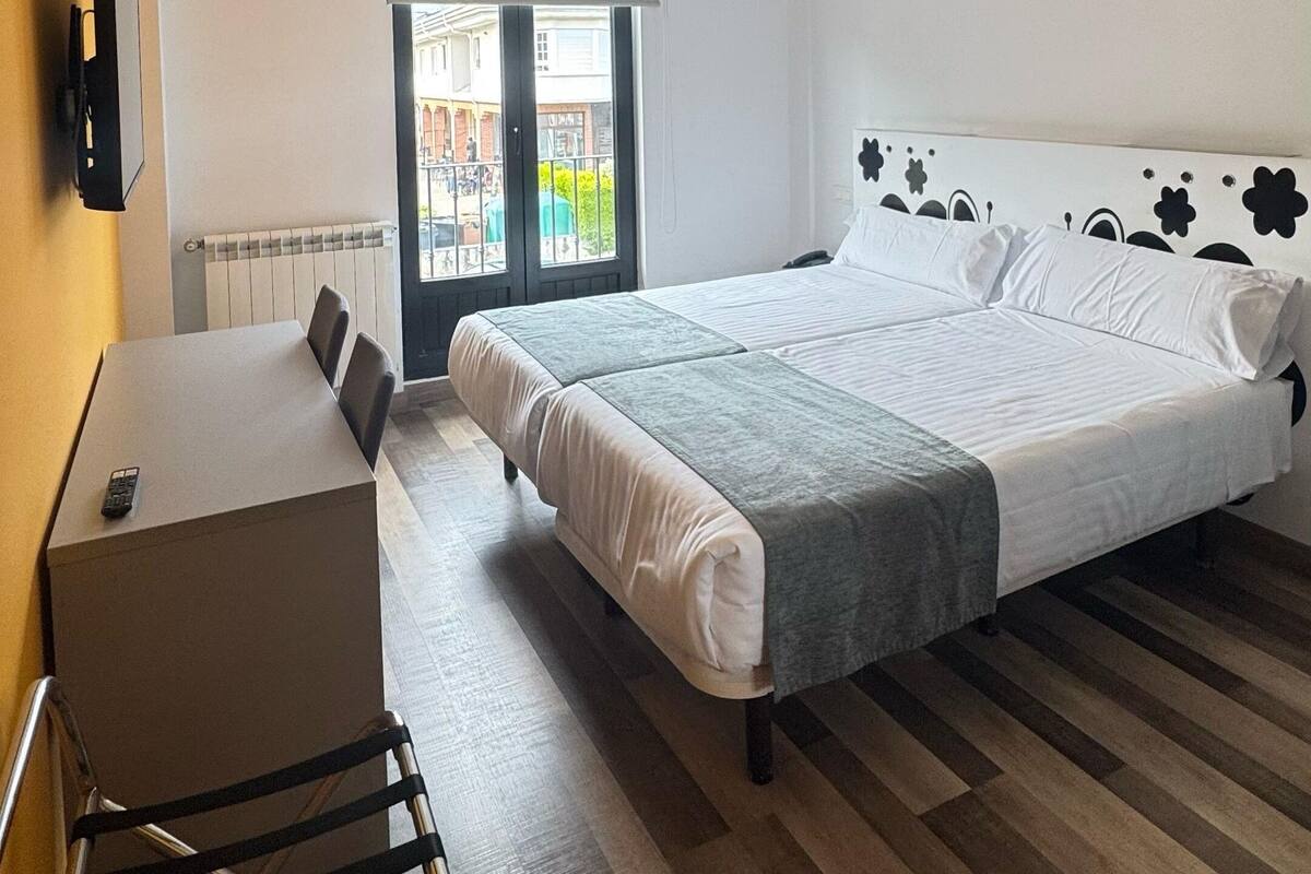 Quarto de hotel com cama, escrivaninha, poltrona, lustre e vista para o exterior.